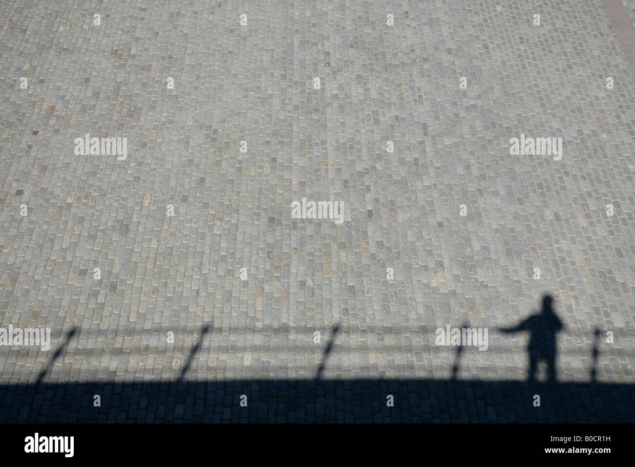 Shadow of man leaning on railings above cobbled square Stock Photo - Alamy