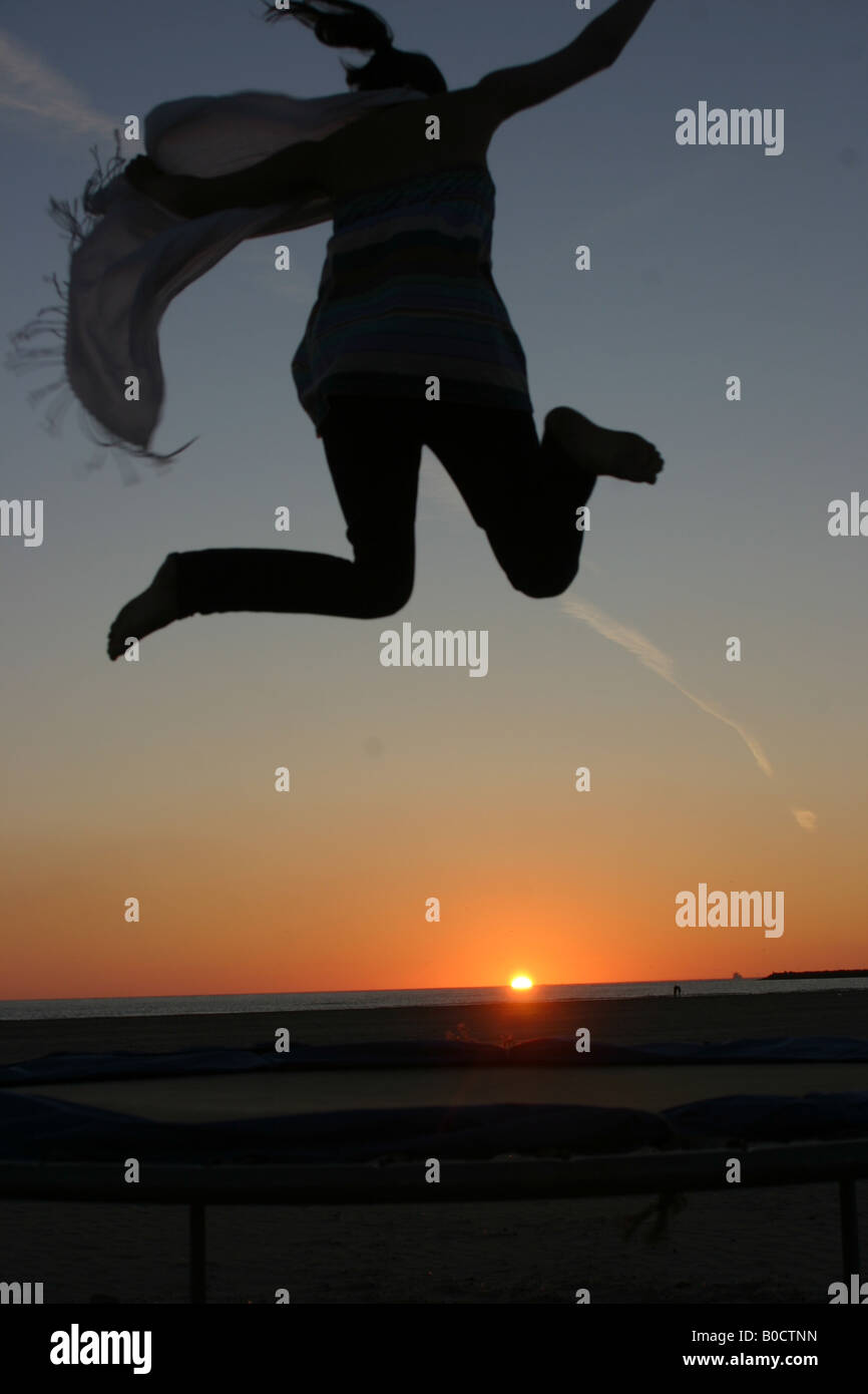 girl jumping in the air with the sun setting over the ocean Stock Photo ...