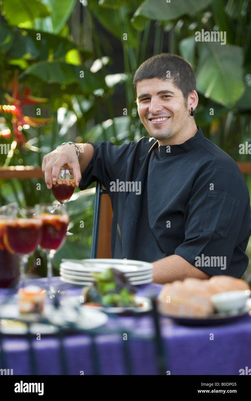 A smiling Spanish chef sits at a colorful table of Mediterranean food ...