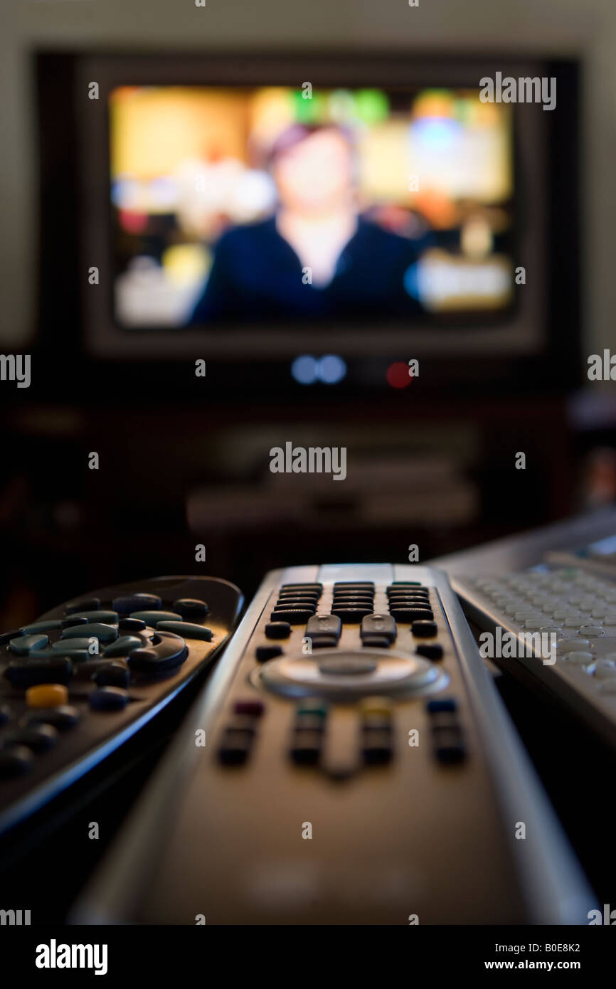 Three remote controls on a table with a TV in the background Stock ...