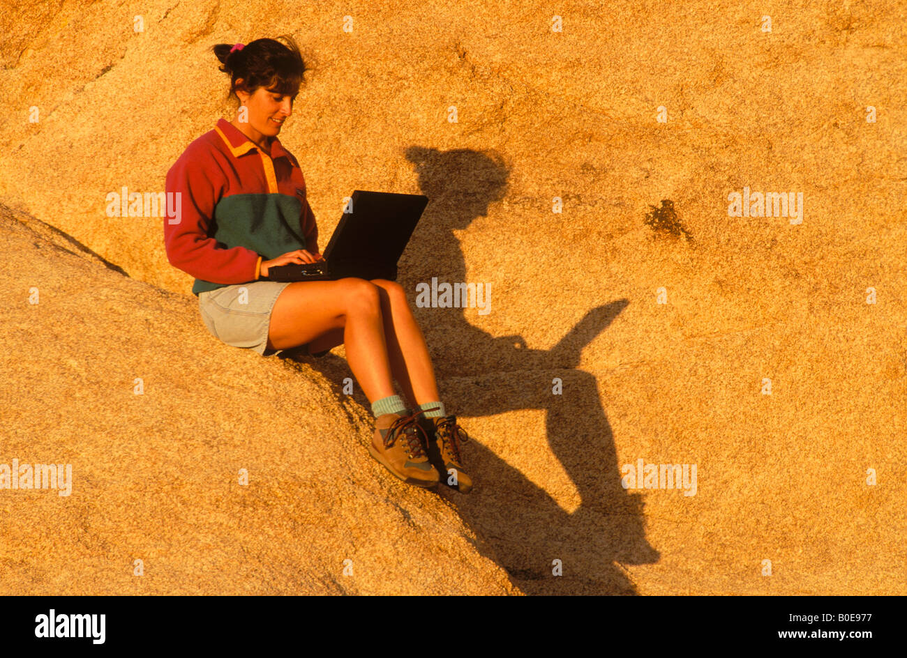 Warm evening light on woman sitting on boulder using a laptop computer ...