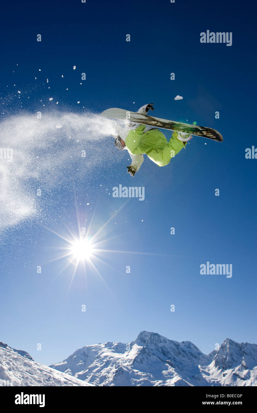 Snowboarder spinning of jump over sunny snowy mountainside Stock Photo ...