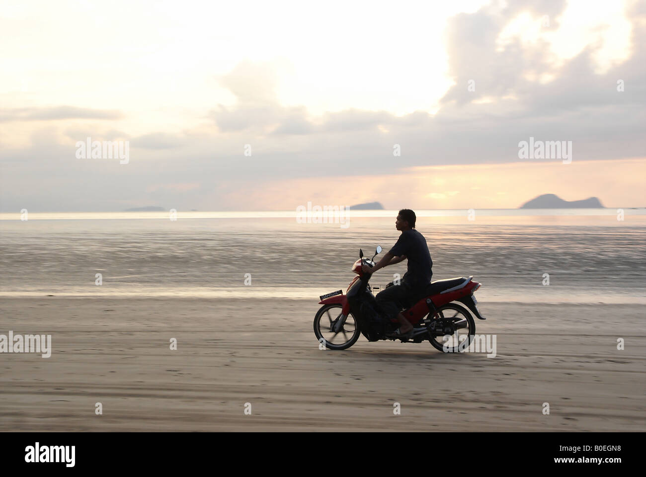 A motorcyclist riding along the beach at sunset Stock Photo - Alamy