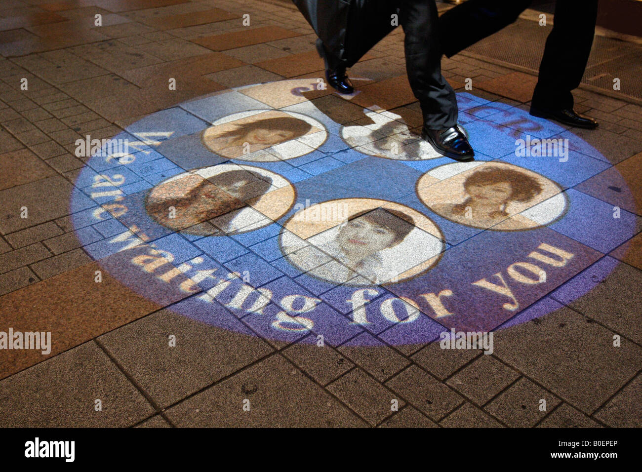 Businessmen walk by an advertisment projected onto the pavement Stock ...