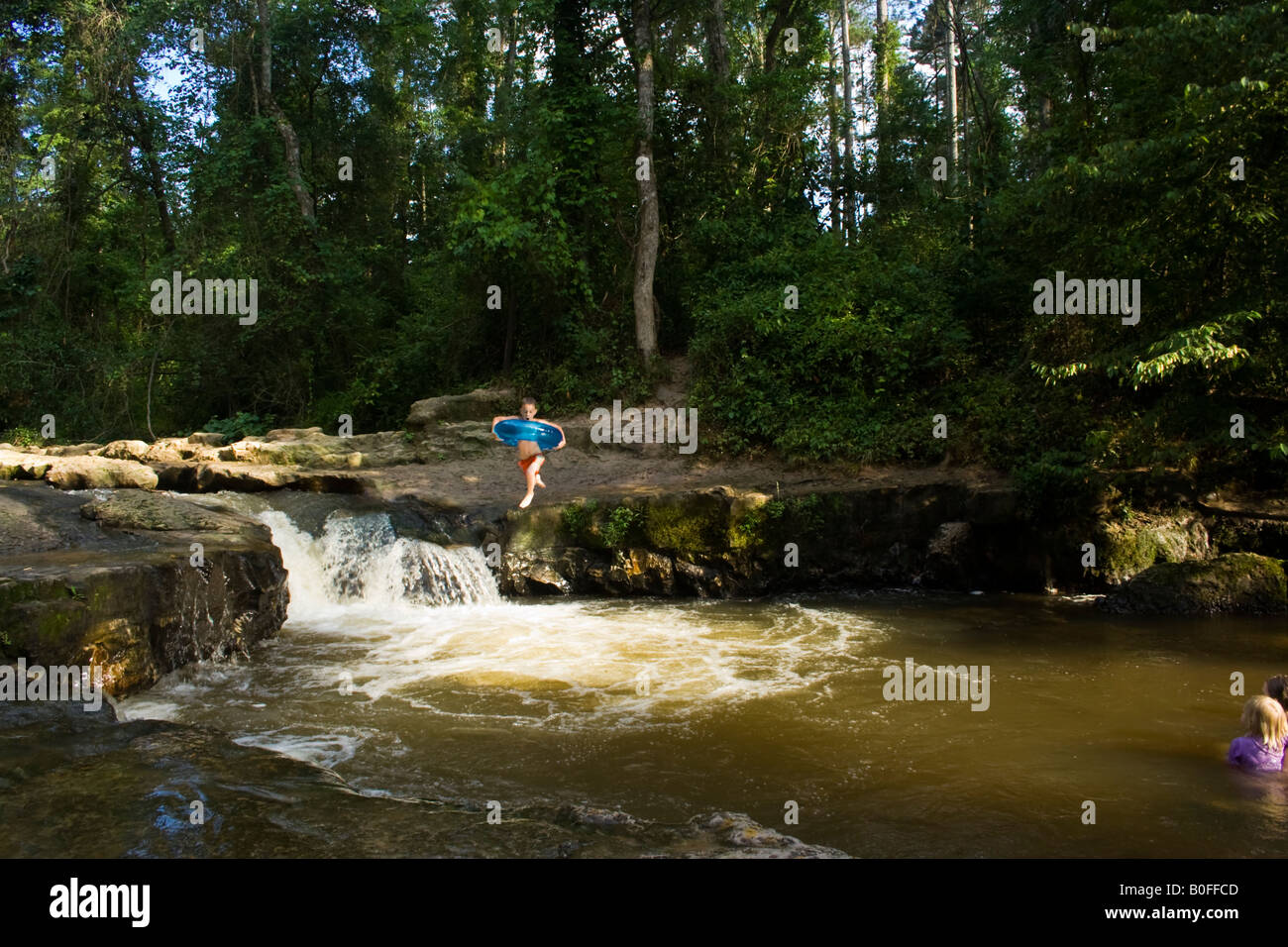 Boy jumping into water below a waterfall with intertube Stock Photo - Alamy