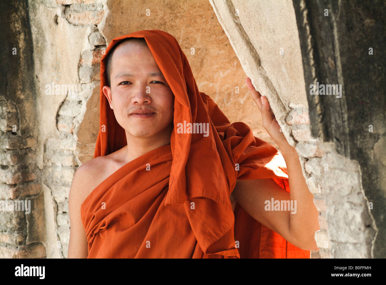 A Buddhist monk dressed in bright orange robes stands in the archway at ...