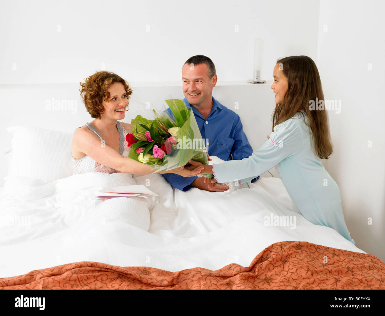 Girl giving mother flowers in bed Stock Photo - Alamy