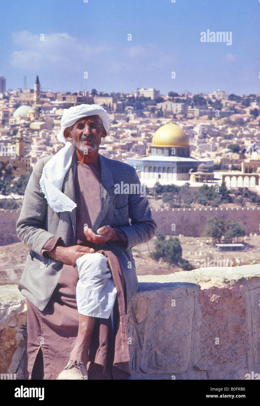 elder scruffy male seated on a stone wall with the Dome of the Rock and ...