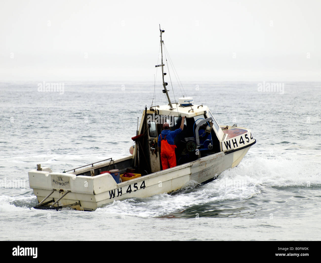 Fishing boat and crew heading out to sea on a grey day Stock Photo - Alamy