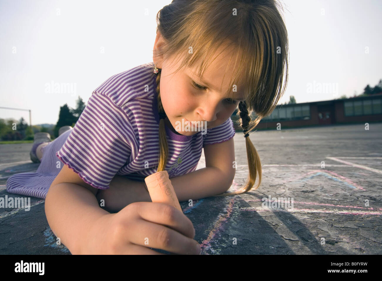Young girl laying down on pavement drawing with chalk Stock Photo - Alamy