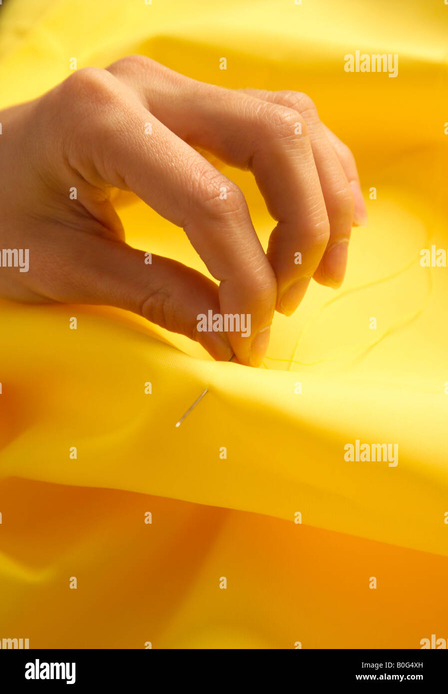 Hand sewing needle and thread through yellow cloth Stock Photo - Alamy