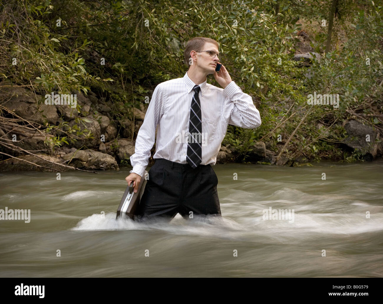 man in business attire and briefcase standing mid-stream in a river on ...