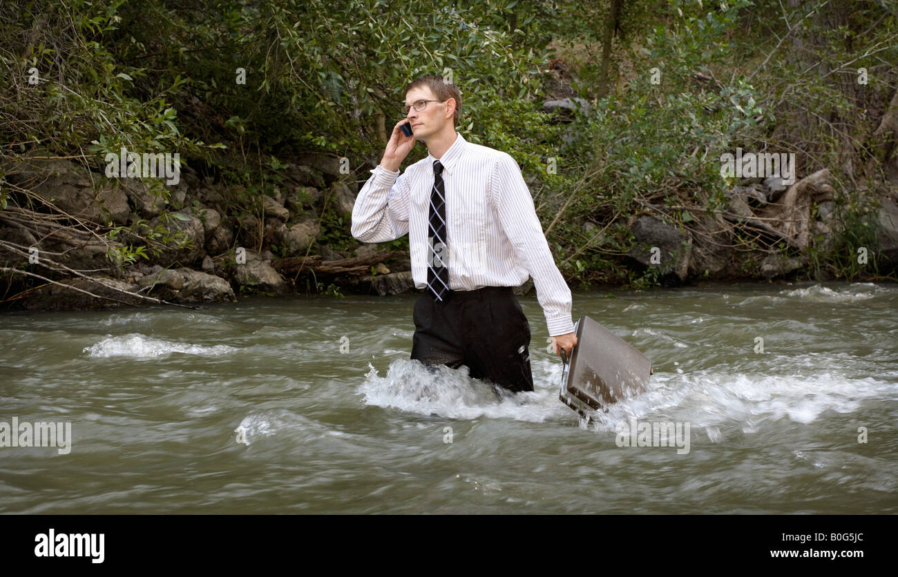 man in business attire and briefcase wading upstream in a river on his ...