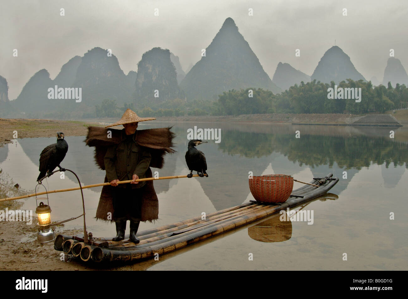 Li River fisherman wearing palm leaf rain cape on bamboo raft with ...