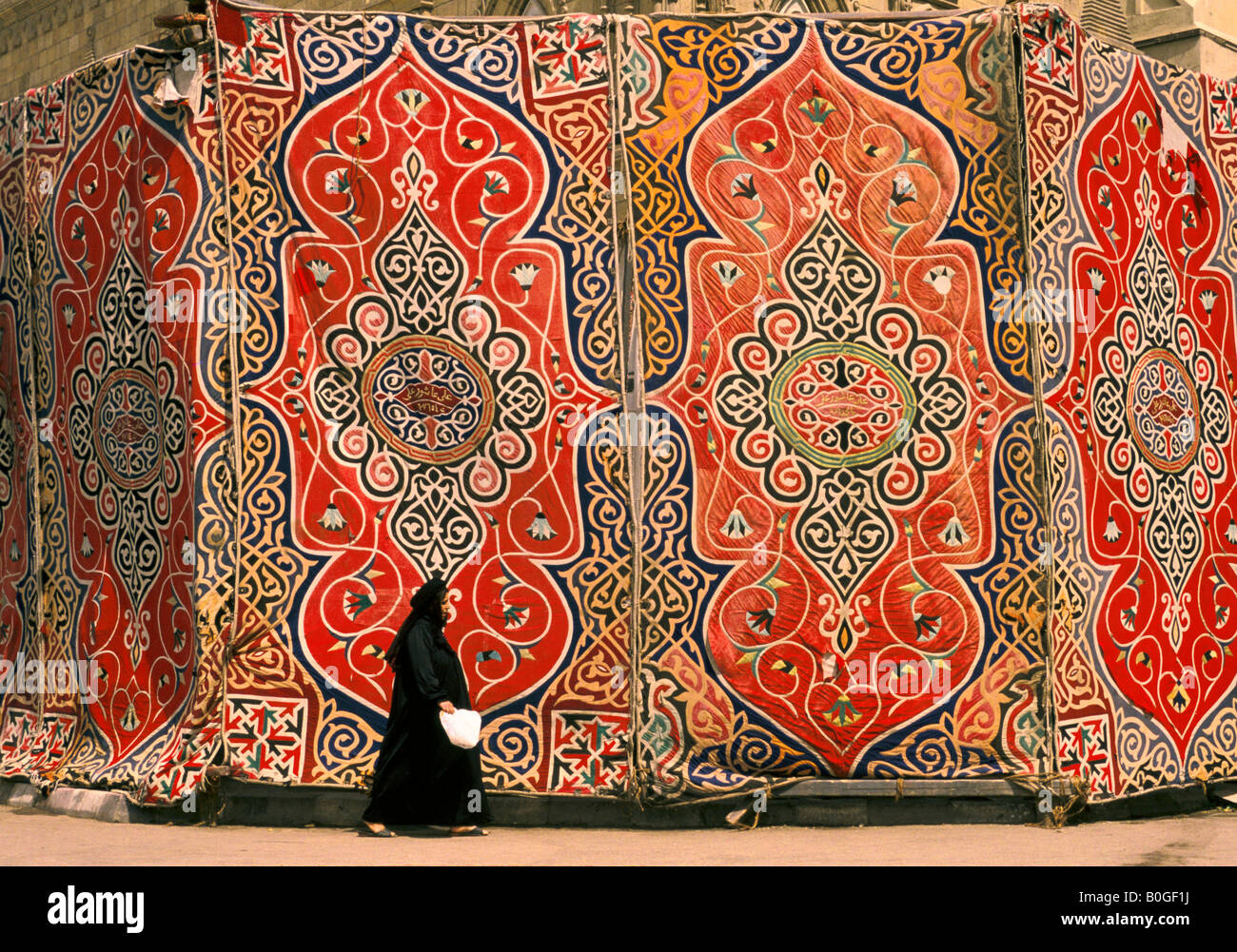 A woman walking past large textiles at El Hussein Mosque, Cairo, Egypt ...