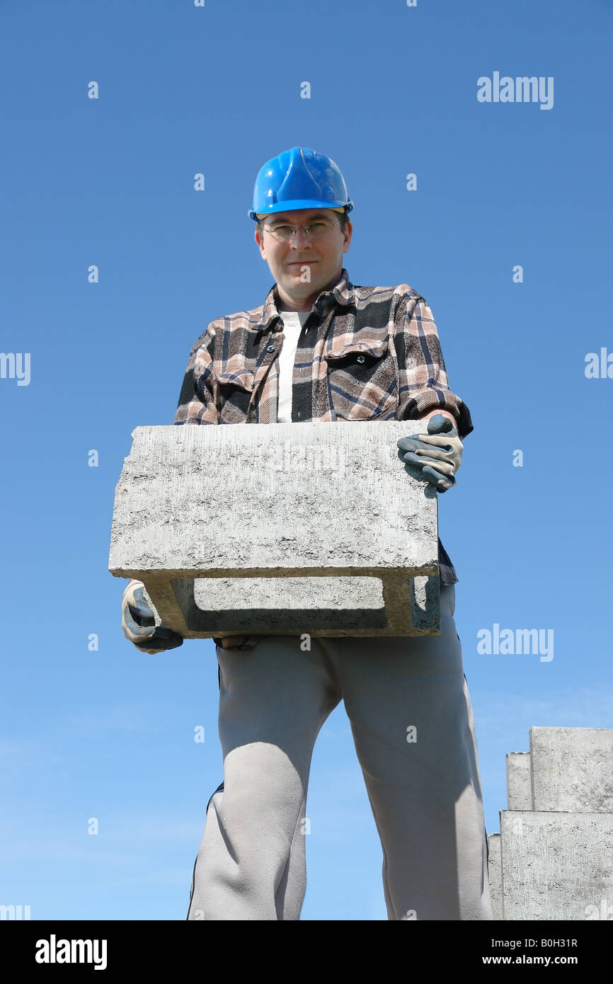 Construction worker in blue hard hat carrying concrete shuttering block ...
