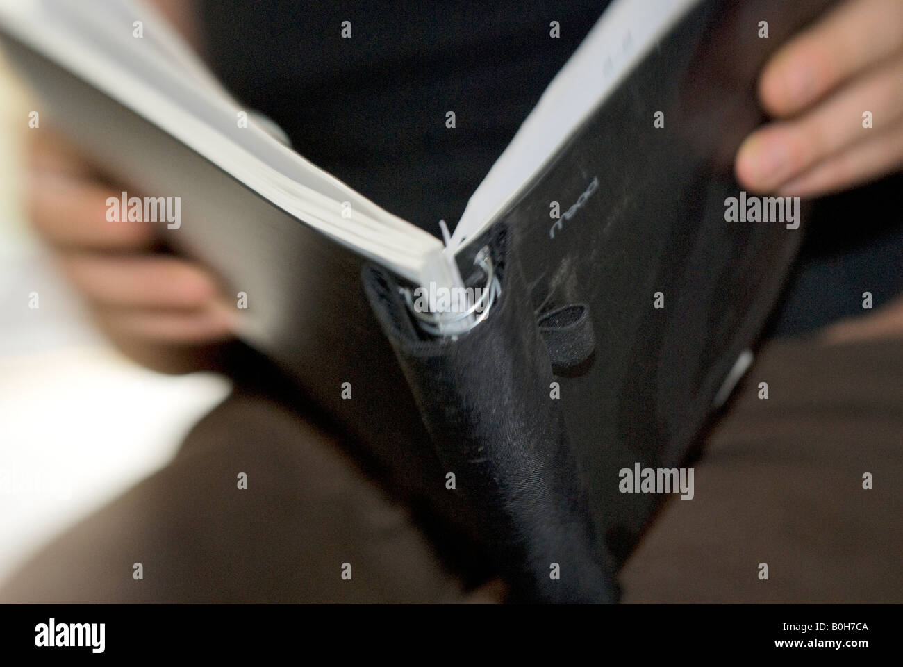 two hands holding a black covered spiral bound notebook open for better ...