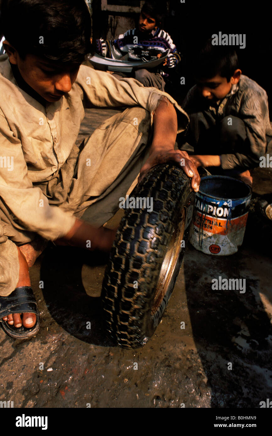 A young child working in a garage helping a mechanic to change a tyre ...