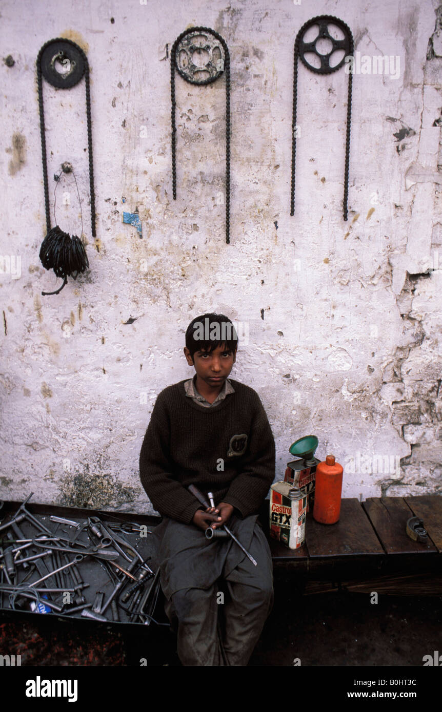 A young boy holding tools, working in a motorcycle repair workshop ...