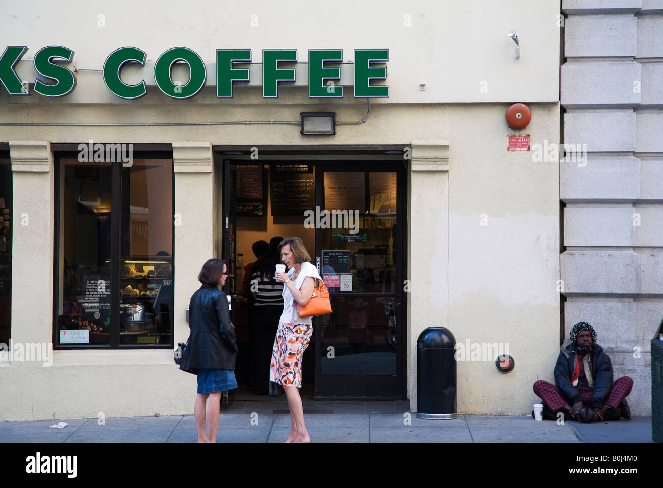 Two woman talking outside a coffee bar with a begger person sat outside ...