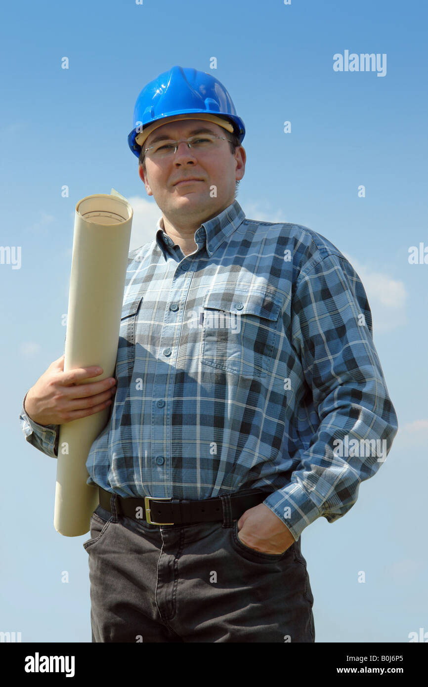 Civil engineer wearing blue helmet posing with roll of building plan ...