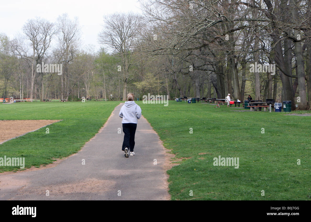 A woman taking a walk on a paved path in a well groomed park Stock ...