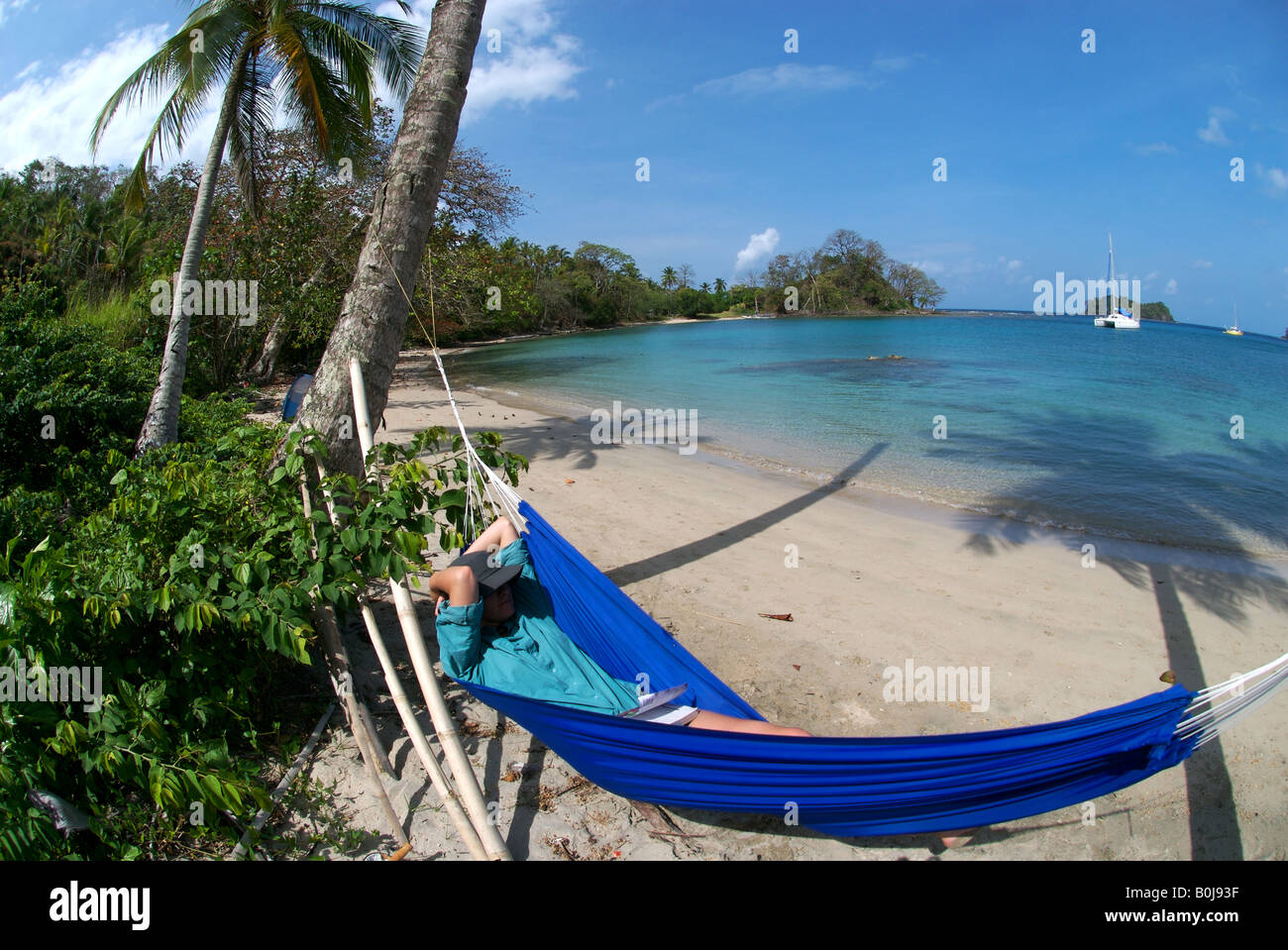A woman takes a nap in a hammock on a remote beach with a sailboat ...