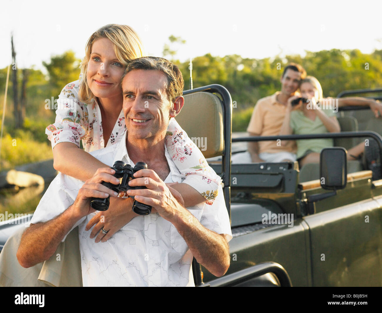 Two couples on trip, one sitting in jeep, using binoculars Stock Photo ...