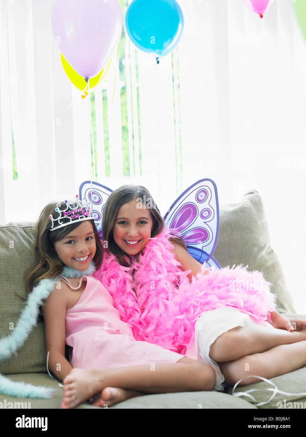 Portrait of two girls (7-9, 10-12) sitting on sofa in party costumes ...