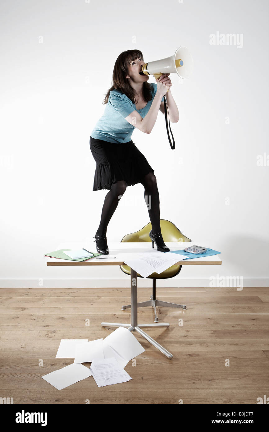 Woman standing on desk, shouting through megaphone Stock Photo - Alamy