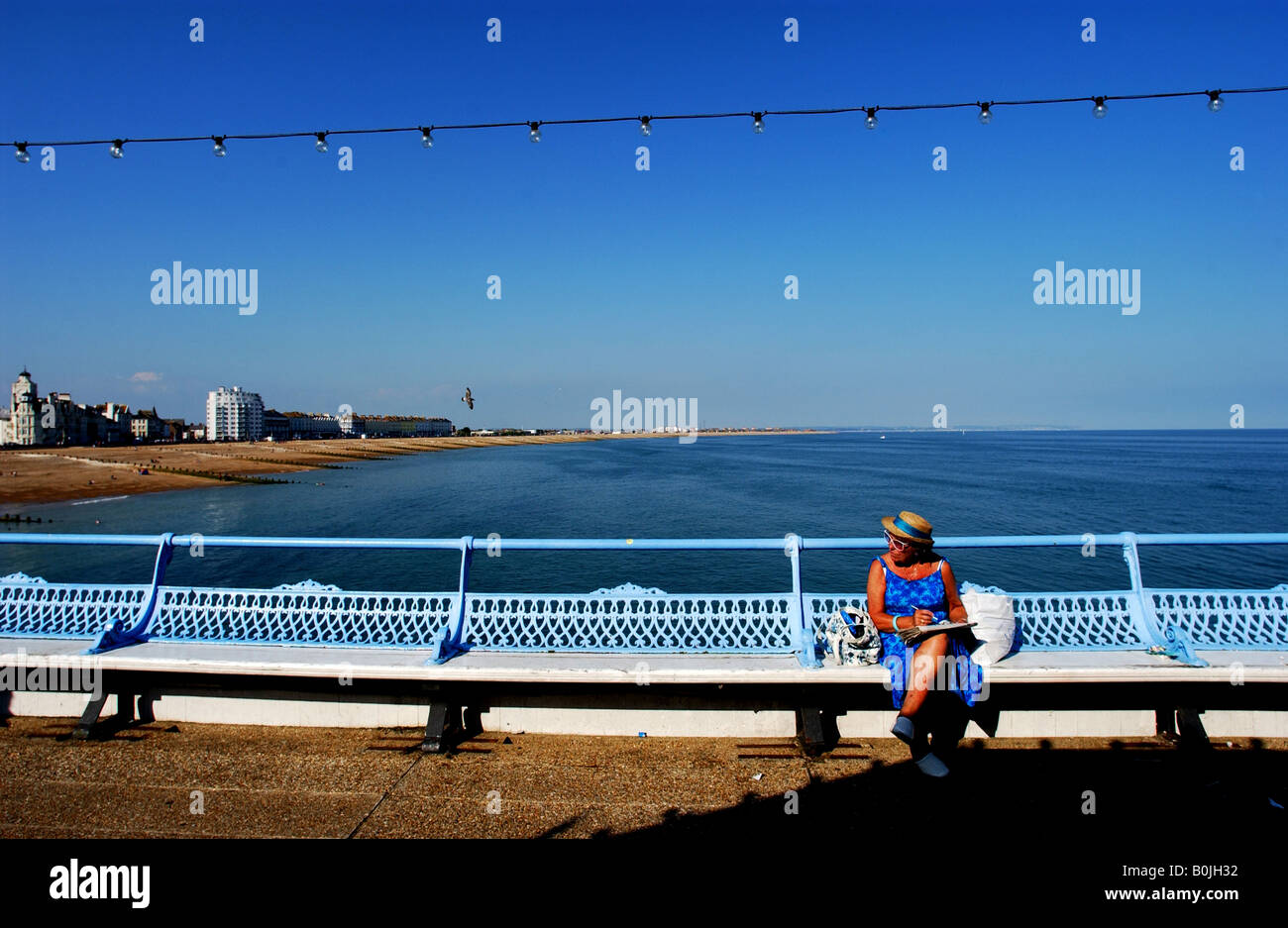A woman reads a book on Worthing Pier, England on a cloudless sunny day ...