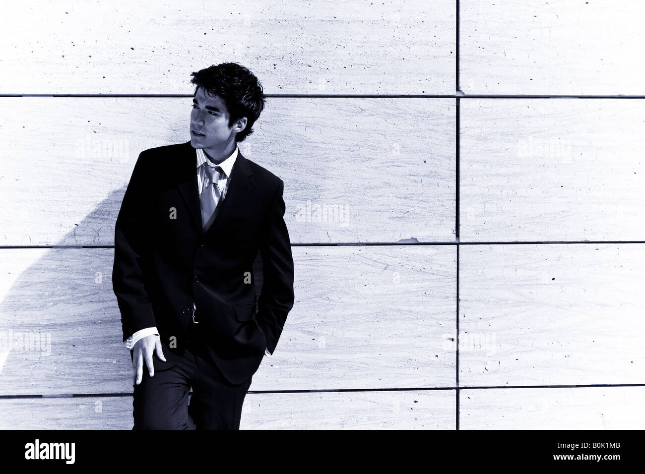 Lone businessman posing on wall blue toned Stock Photo - Alamy