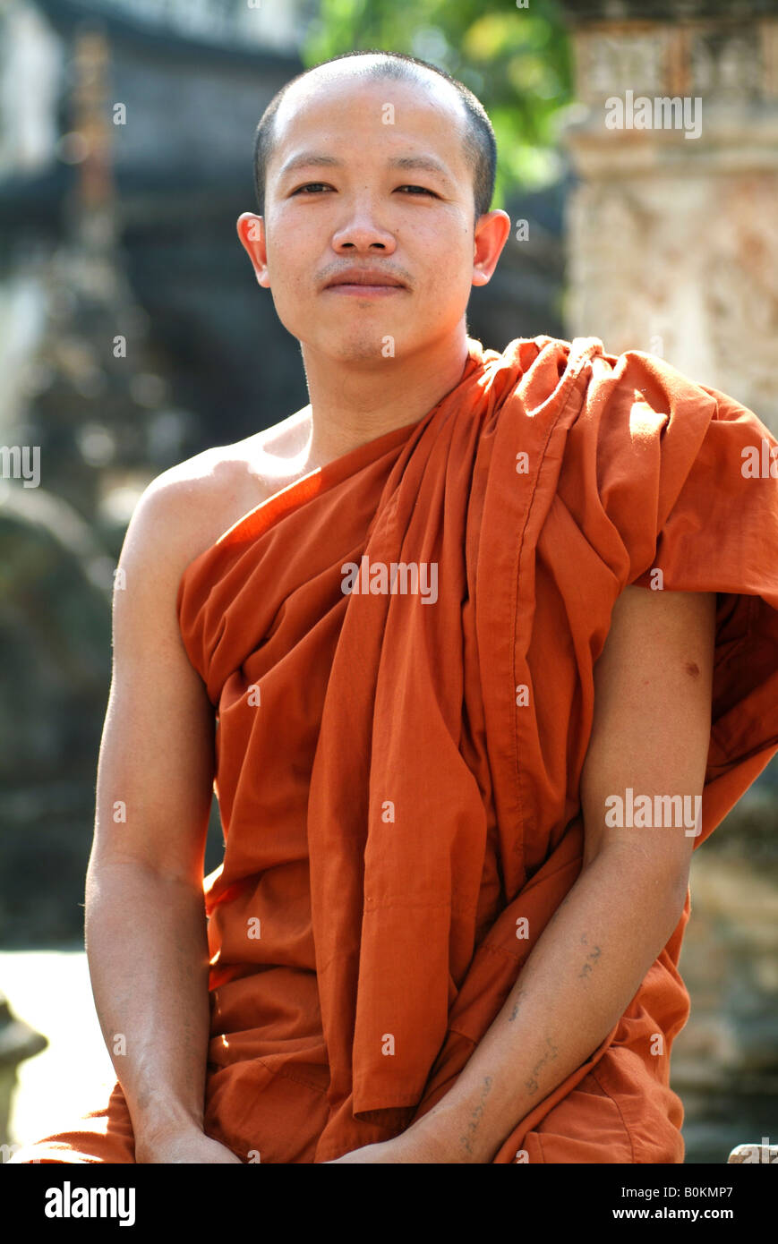 A Buddhist Monk stands in an ancient temple grounds with orange robes ...
