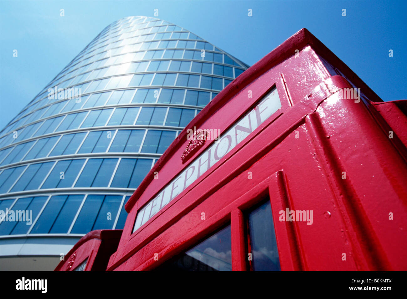 A traditional red telephone box with glass fronted City building in ...