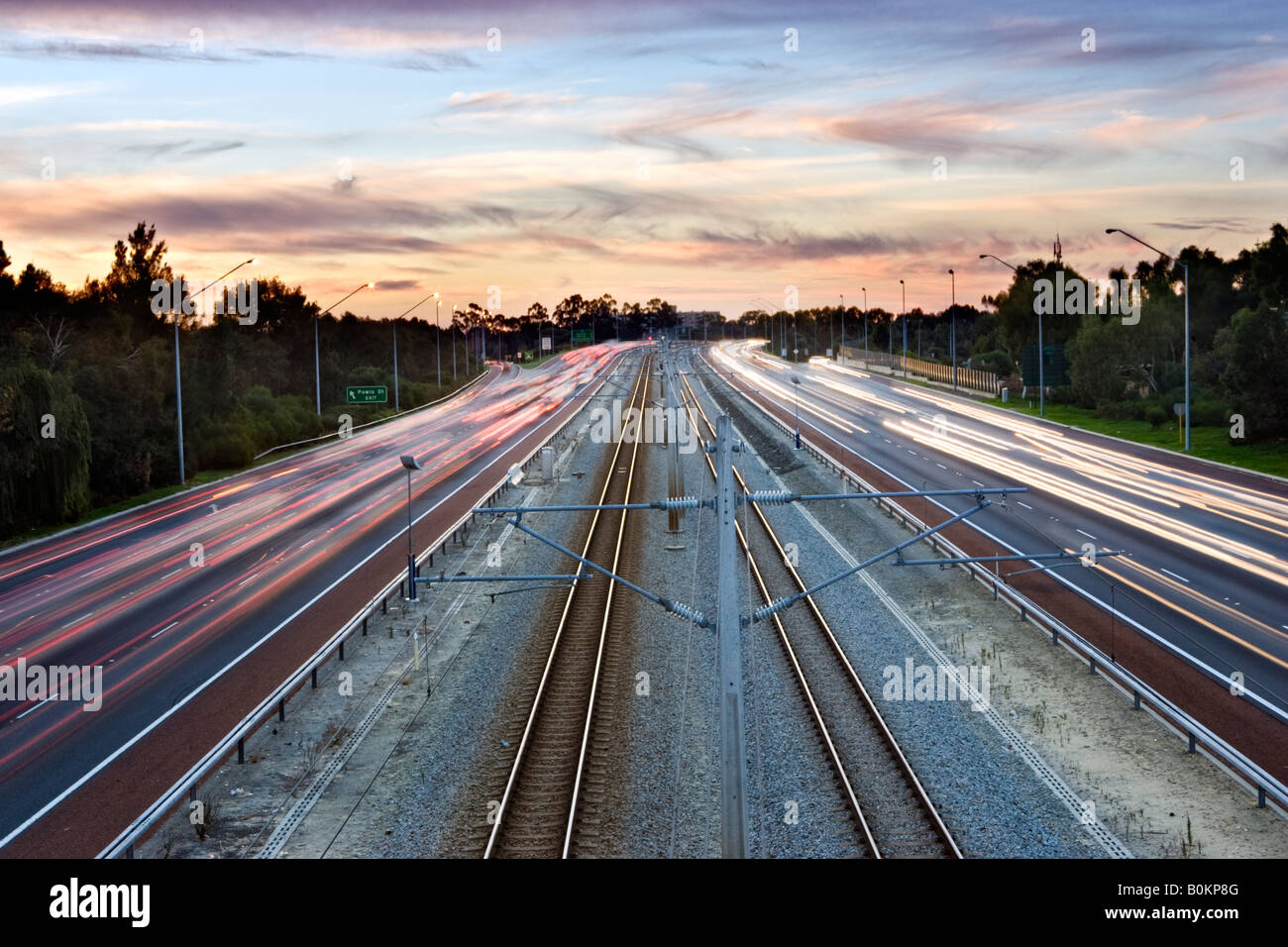 Traffic on the Mitchell Freeway at sunset. A rail track is between the ...