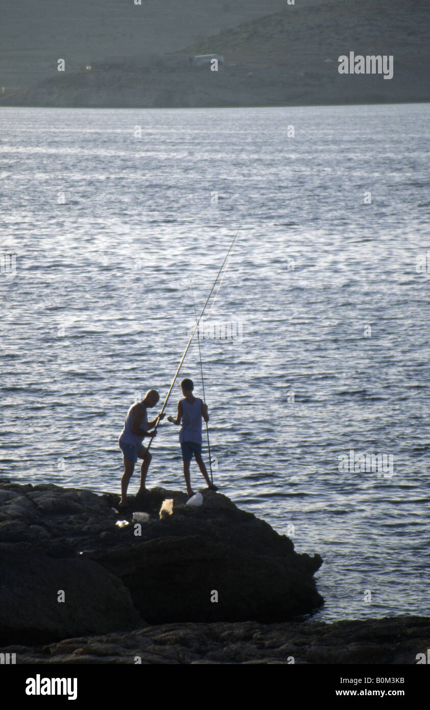 Man and boy fishing off rocks by evening light Stock Photo - Alamy