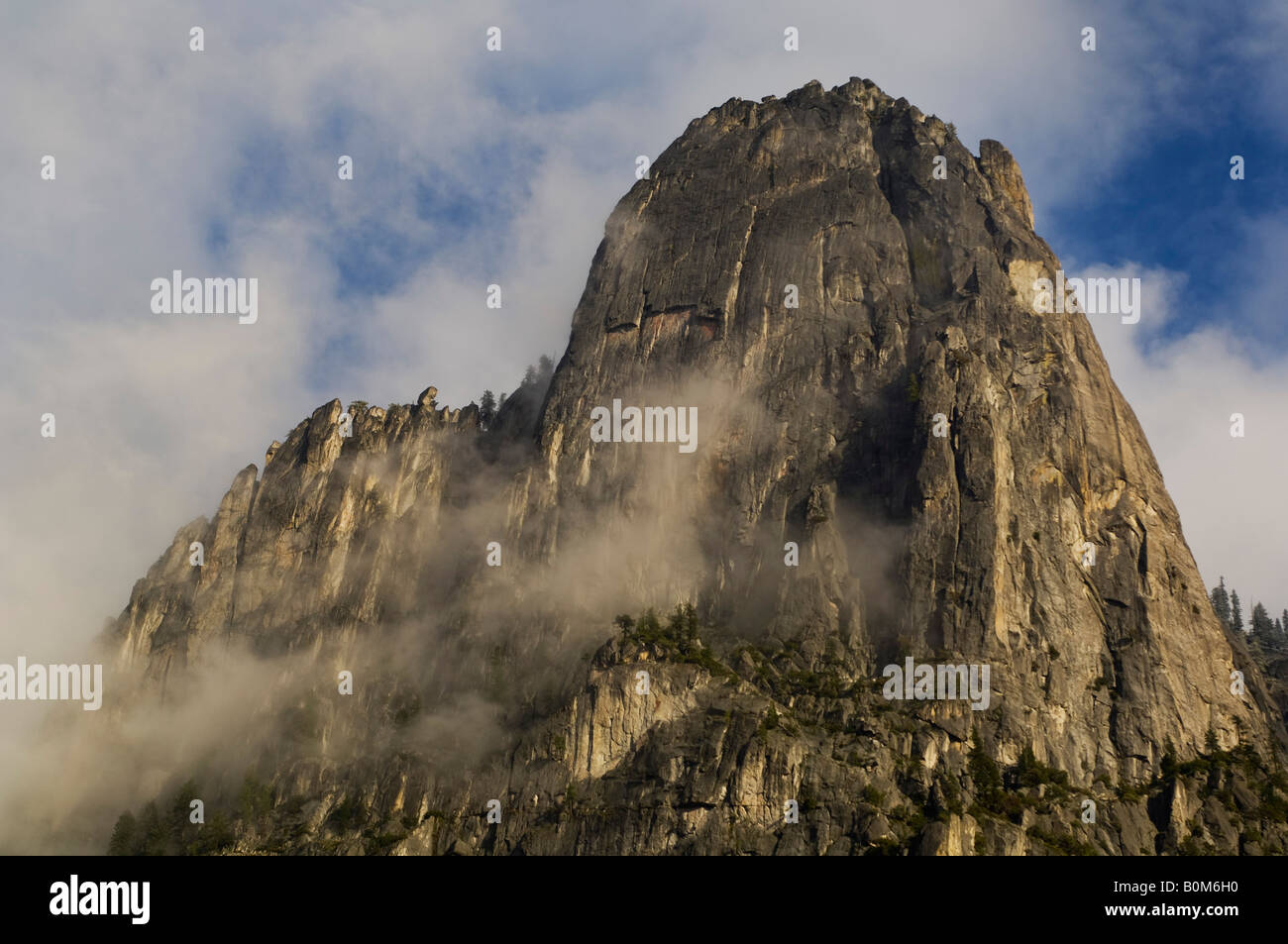 Storm clouds shroud the sheer granite cliff of Sentinel Rock at sunset ...