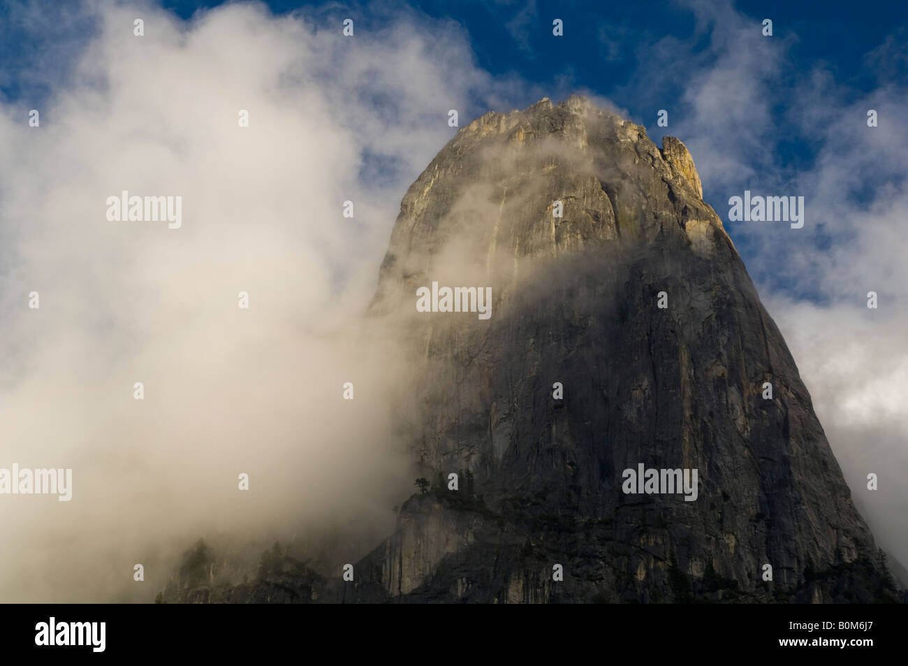 Storm clouds shroud the sheer granite cliff of Sentinel Rock at sunset ...