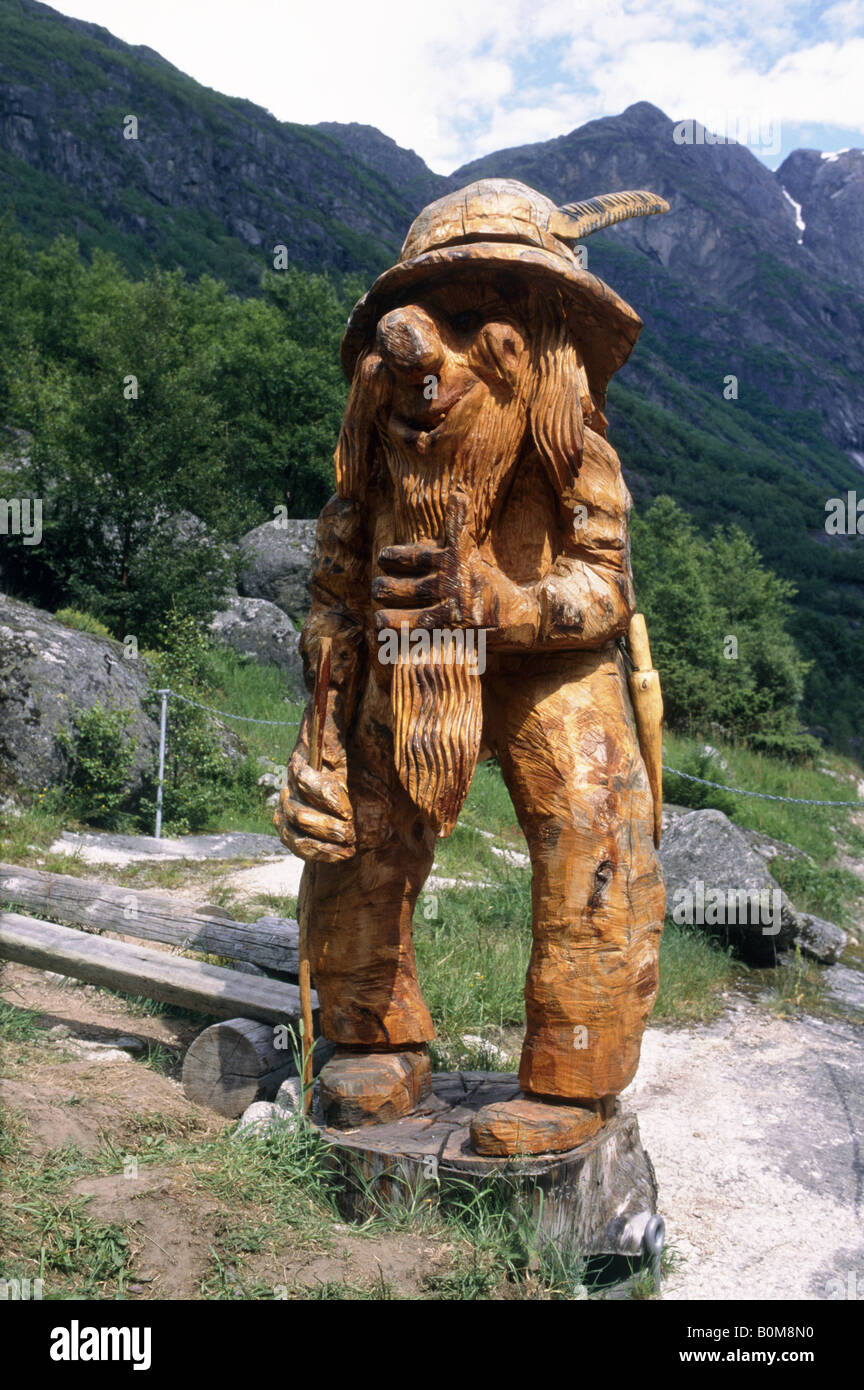 Wooden carved troll with hat holding beard. Mountain scenery in ...