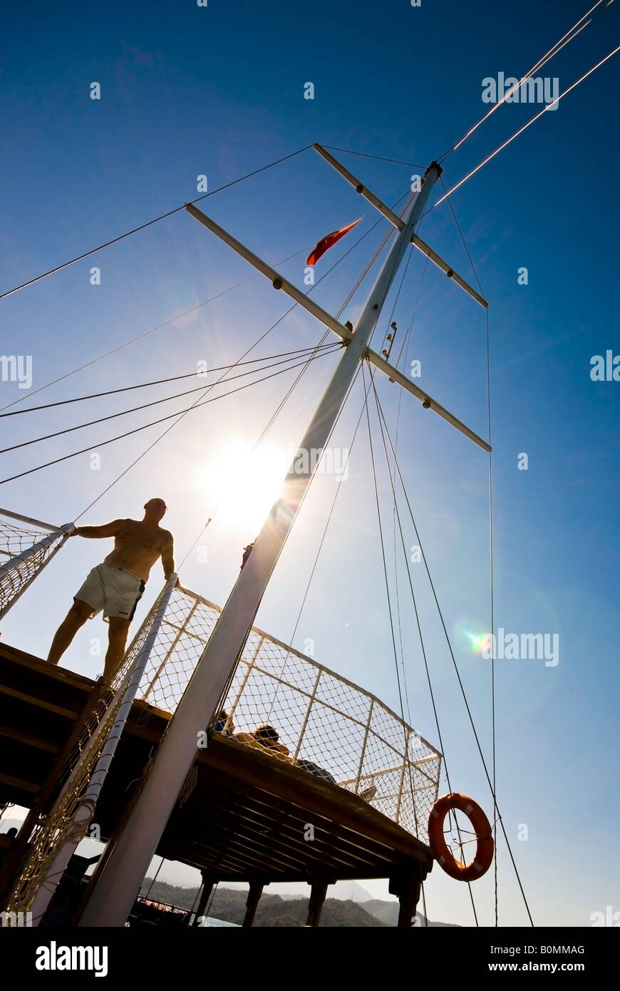 Mast of a boat and a man against bright blue sky with the sun glaring ...