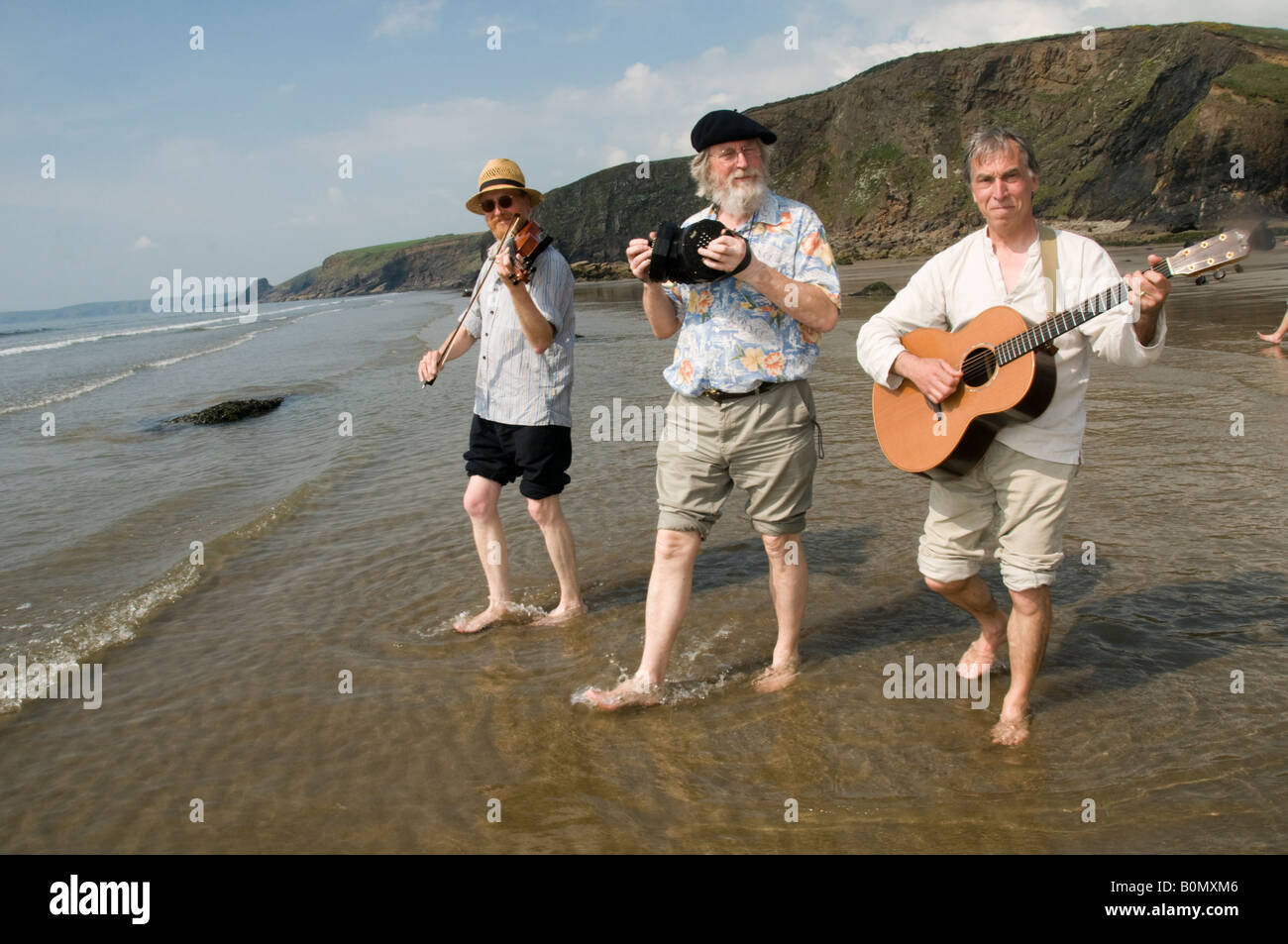 Three traditional acoustic folk musicians playing music on the beach ...
