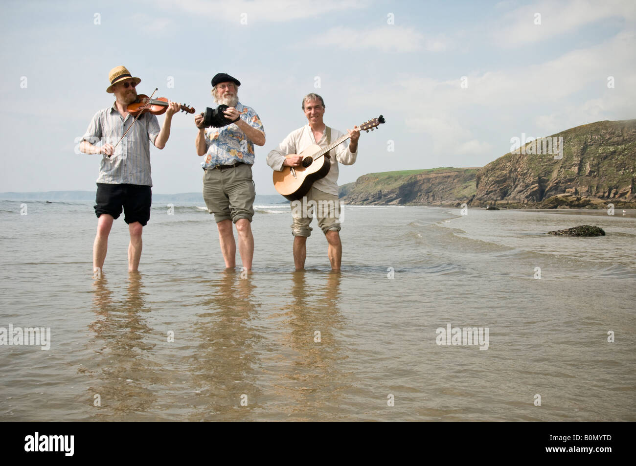 Three traditional acoustic folk musicians playing music on the beach ...