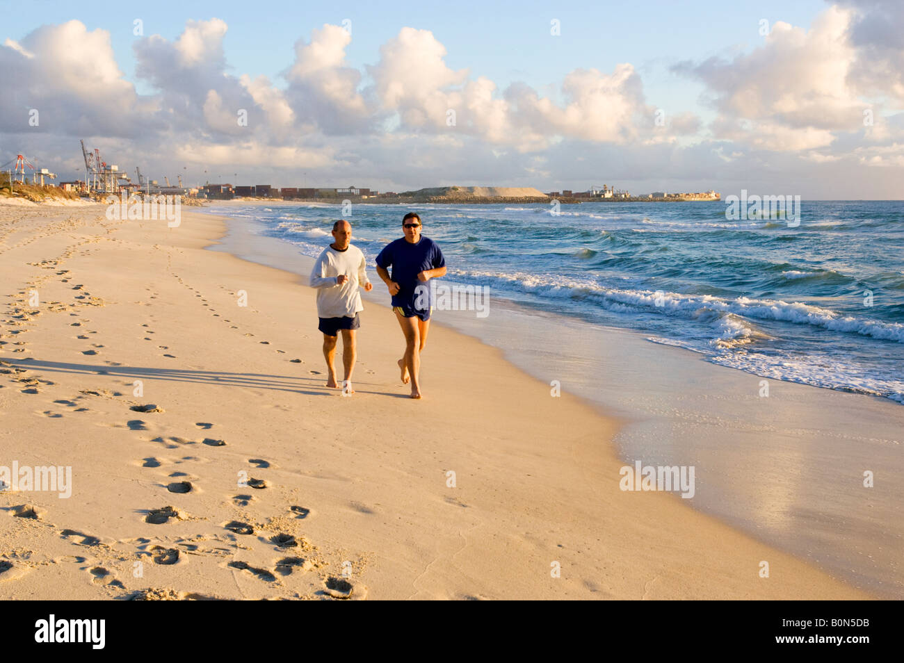 Two men jogging together on the beach in the late afternoon sun ...