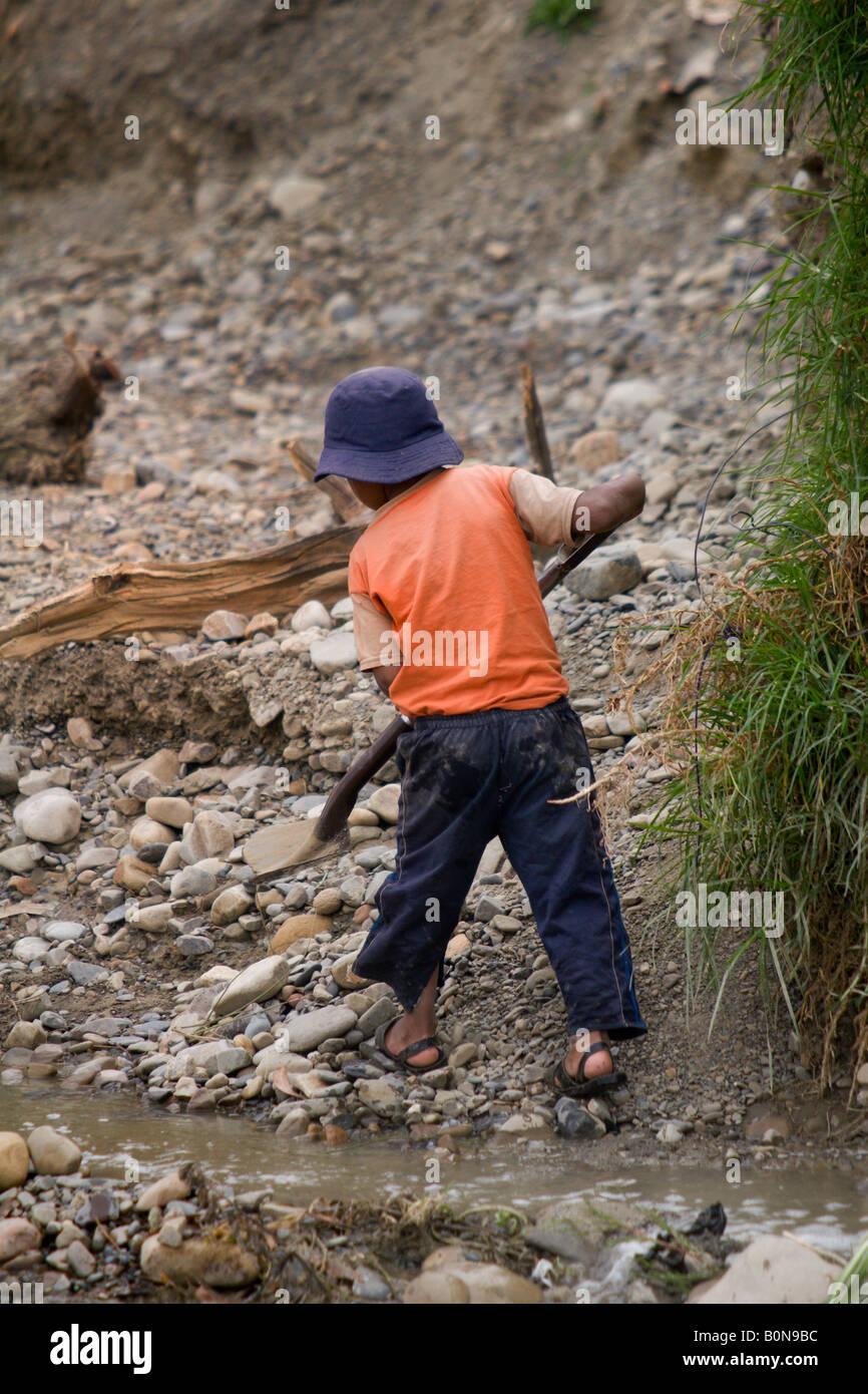 Bolivian child holding a spade to pick sand on a river, to sell it for ...