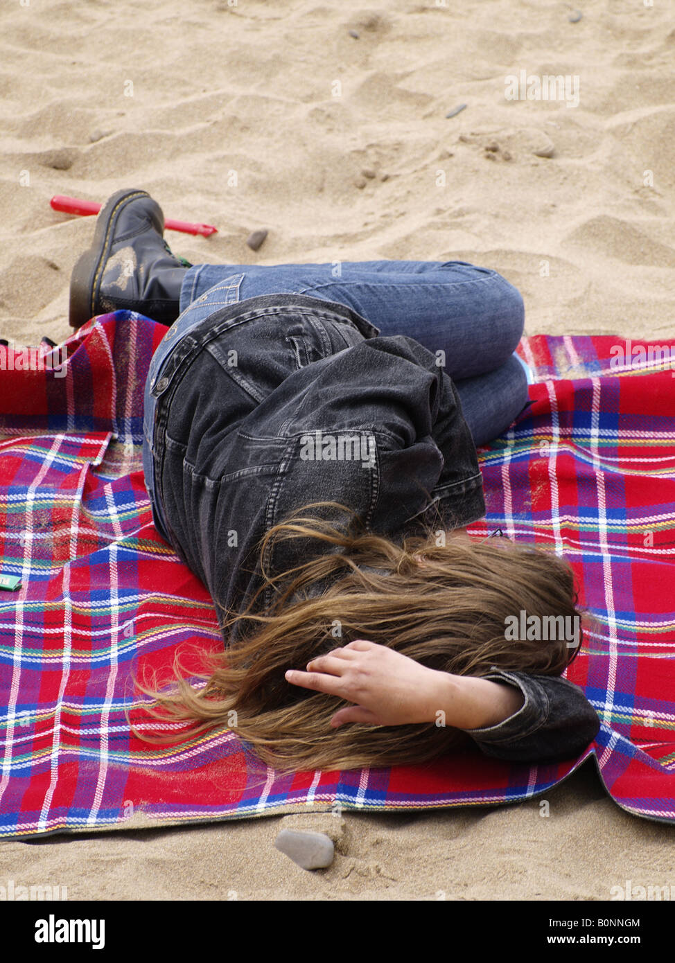 Young woman wearing jeans, jacket and boots, laying on a red checked ...