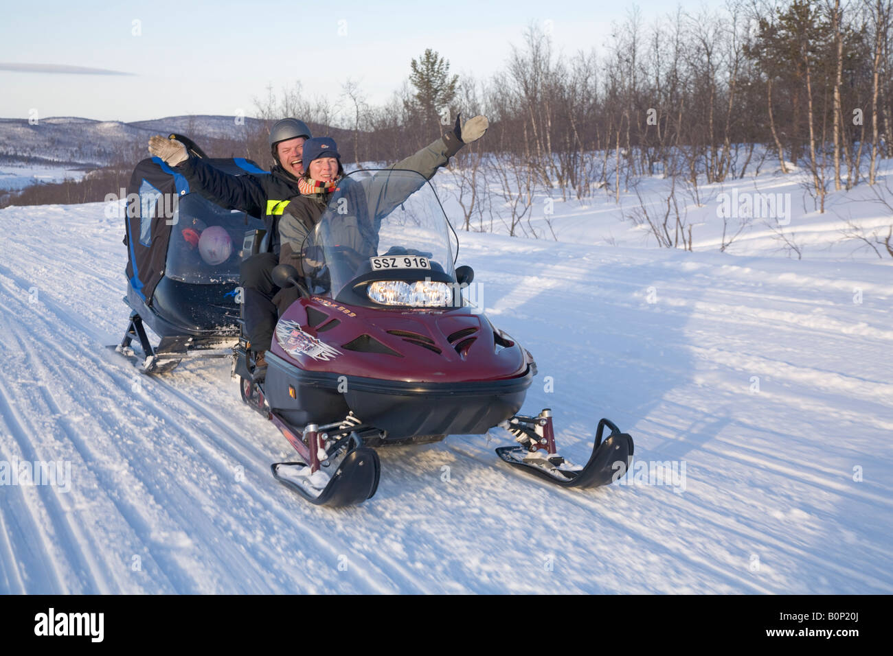 A man and a woman in their fourties ride a Lynx snowmobile in snowy ...
