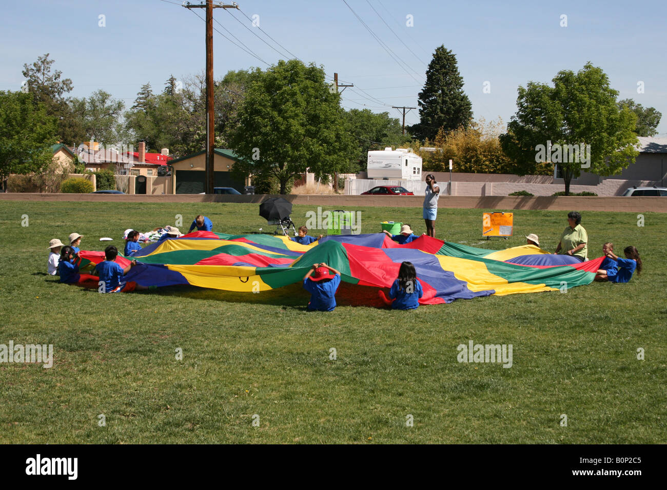 children sitting in circle holding parachute outdoors, field day ...