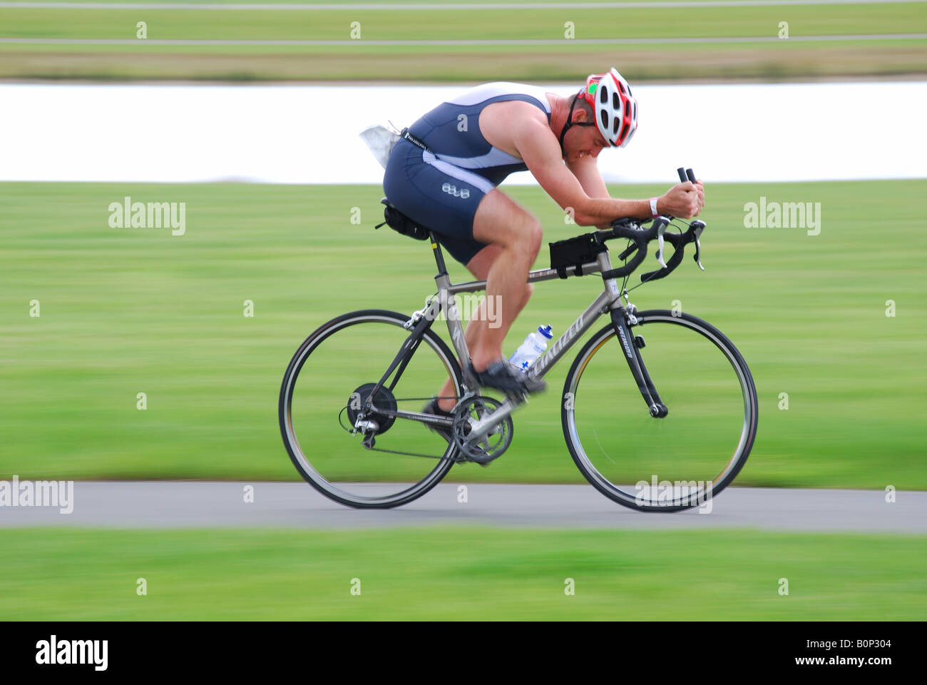 Racing cyclist on track alongside lake, Eton College Rowing Centre ...