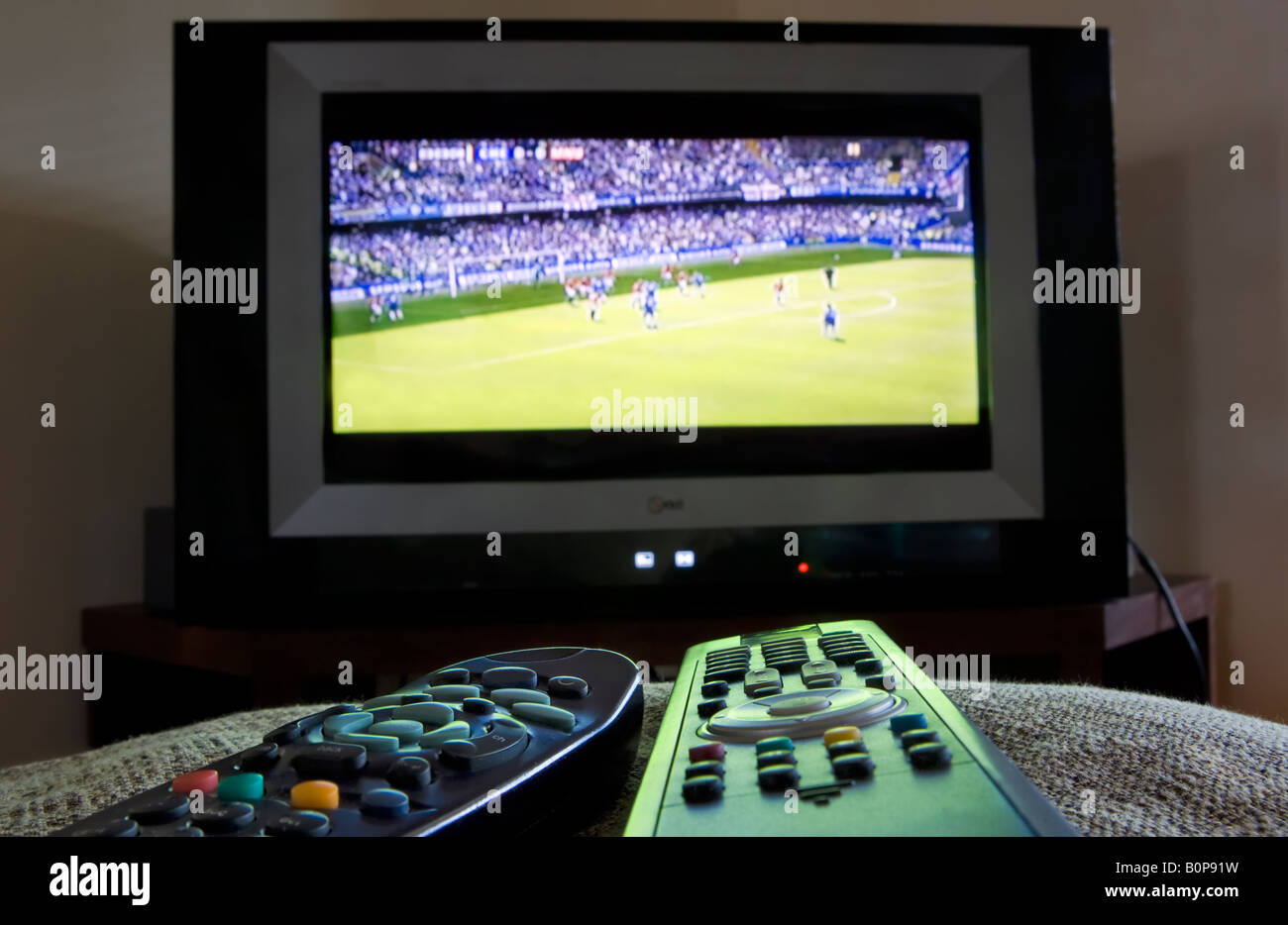TV remote controls on a couch with the football on the TV in the ...