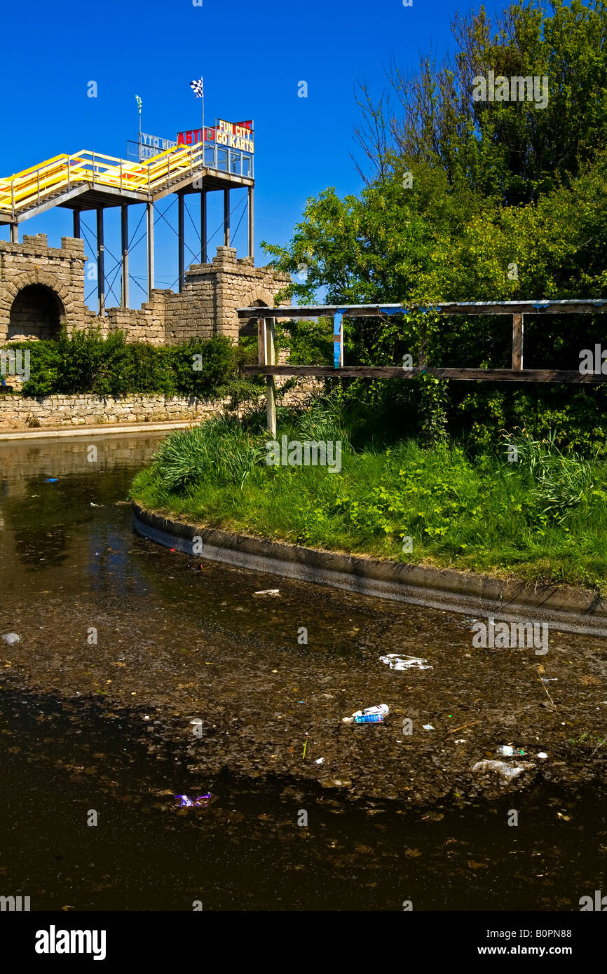 Polluted stream with rubbish and debris floating in the water next to ...